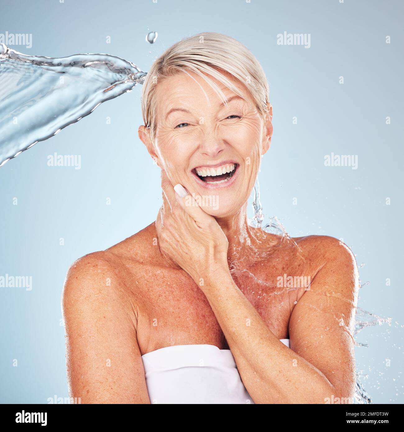 Smile, shower and portrait of a woman with a water splash isolated on a blue background in ...