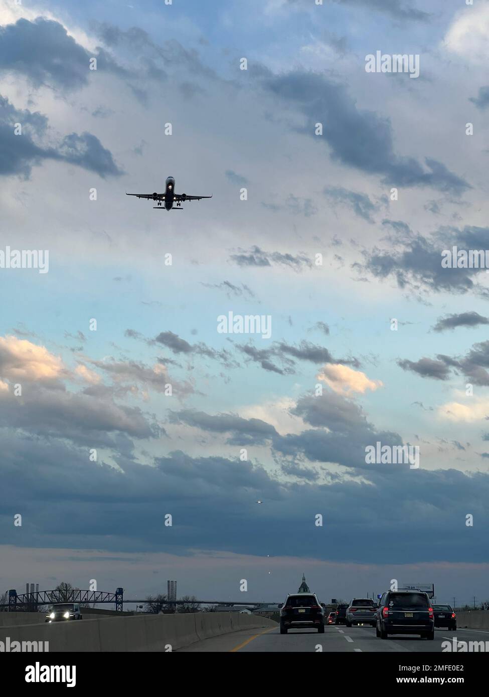 A vertical shot of a plane flying in a cloudy blue sky over cars on ...
