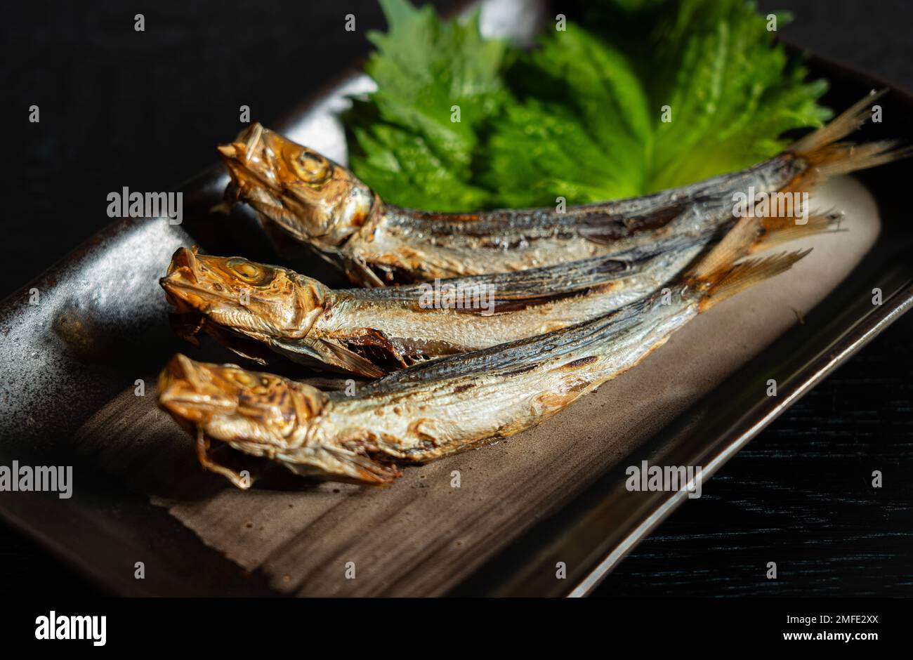 Grilled urume sardines on a black table. A side dish of sake. Japanese ...