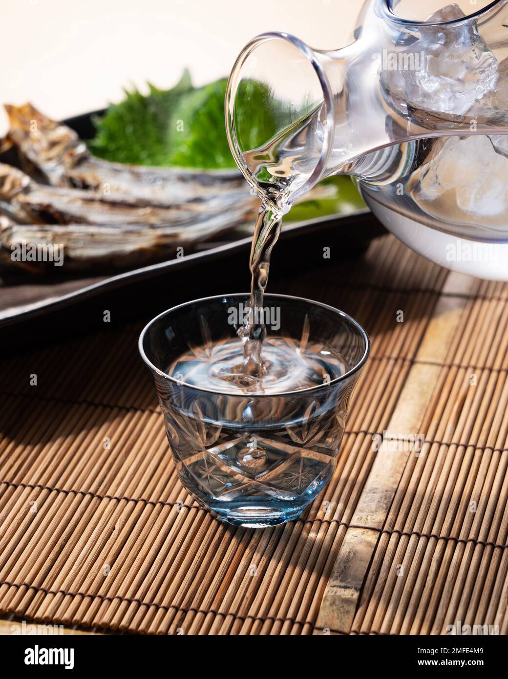 Sake poured into a faceted glass and grilled umeshi sardines placed ...