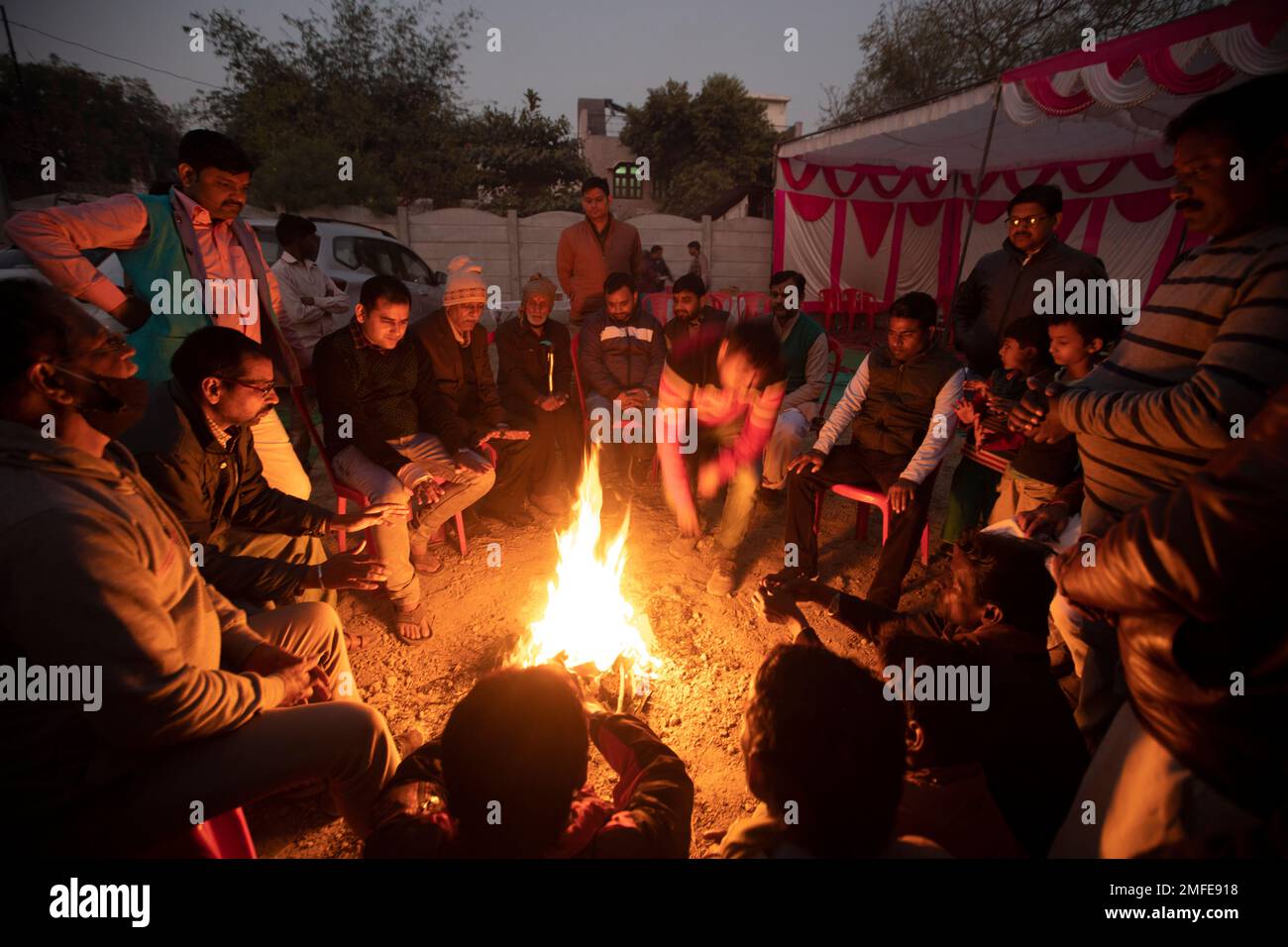 Villagers warm themselves around a bonfire on a cold day, on the ...