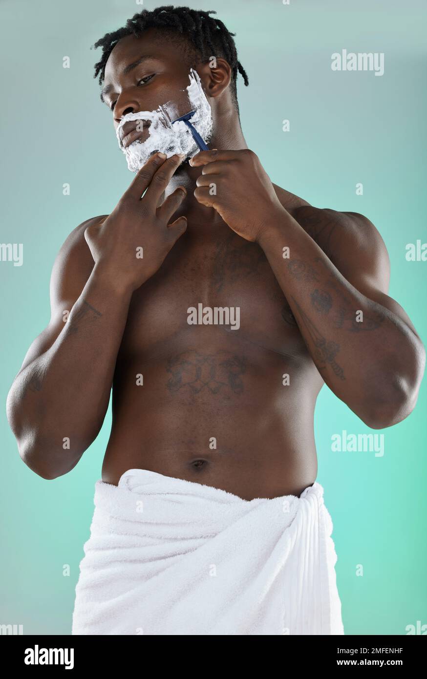 Black man shaving facial hair, skincare cream on studio background and white towel. Happy young ...