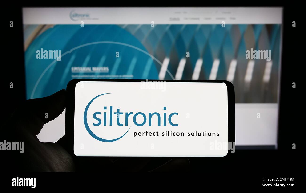 Person holding cellphone with logo of German electronics company Siltronic AG on screen in front ...
