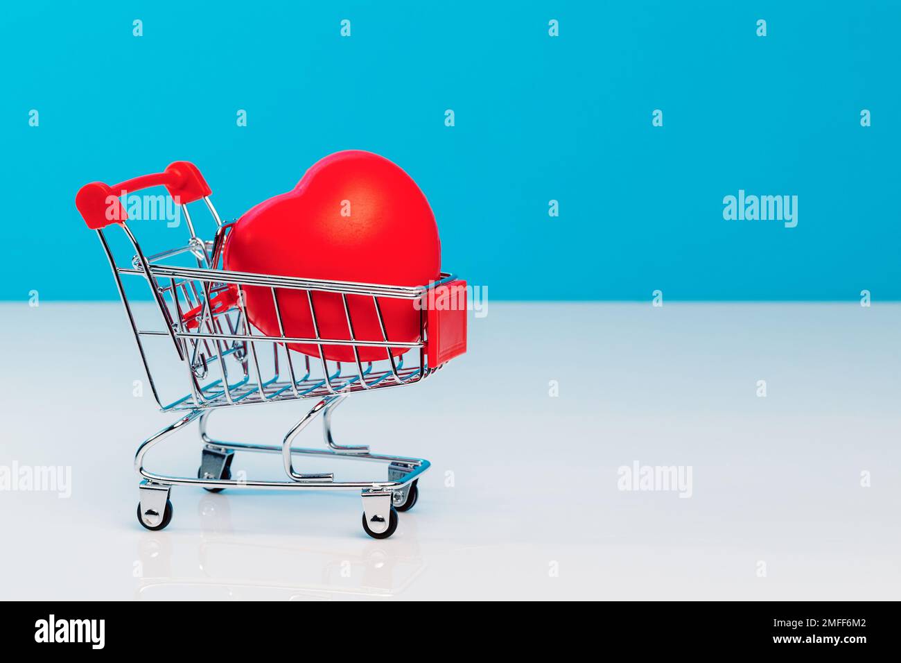 A mini shopping trolley with a red heart shape on a blue studio ...