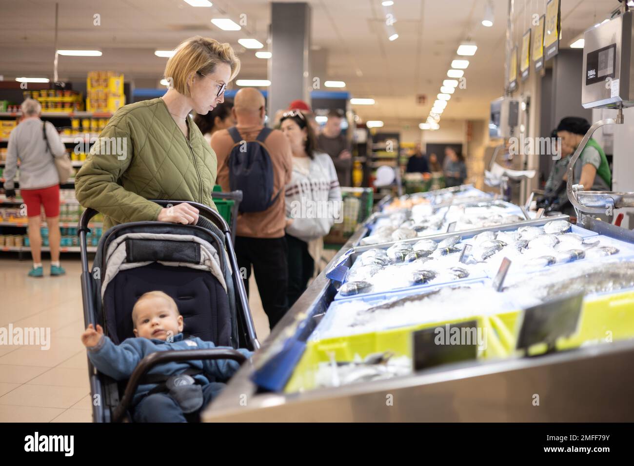 Casualy dressed mother choosing fish in the fish market department of ...