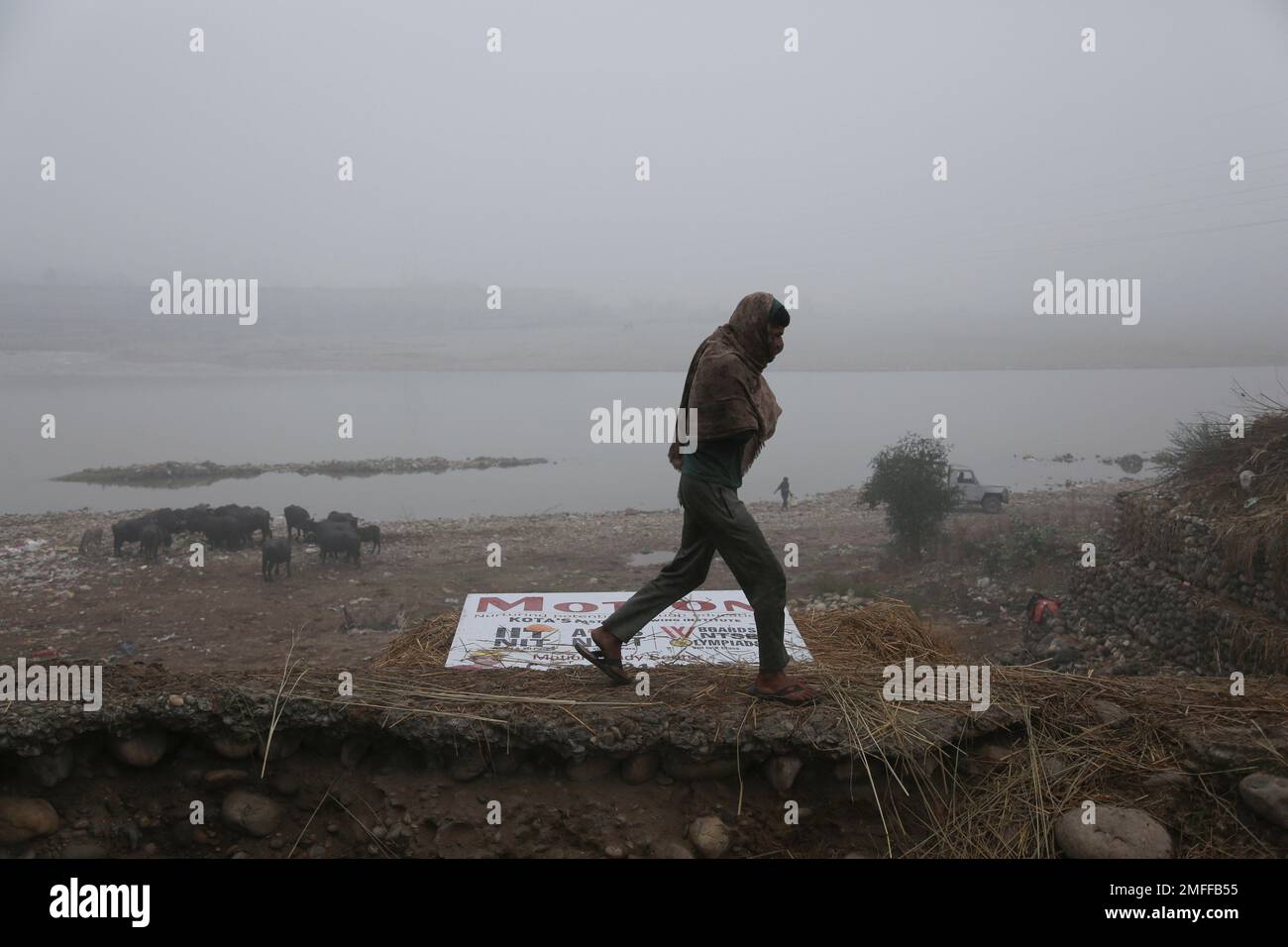 A man covers himself with a woolen shawl as he walks on a cold and ...