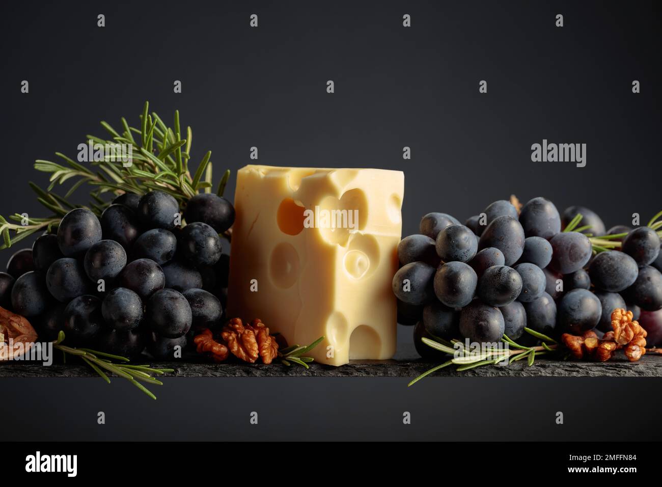 Maasdam cheese with walnuts, blue grapes, and rosemary on a black ...