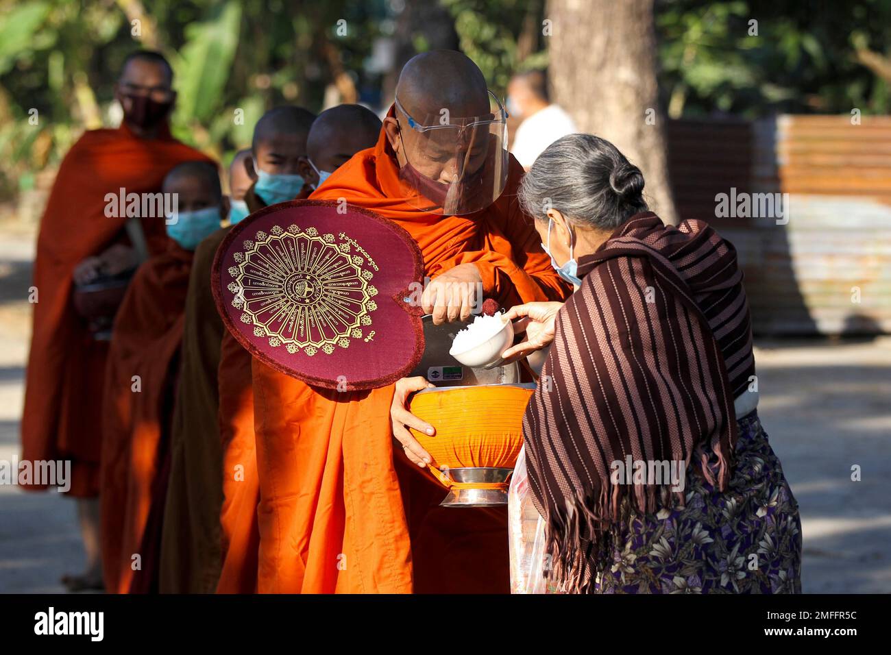 A Buddhist devotee donates alms to a Buddhist monk wearing a face ...
