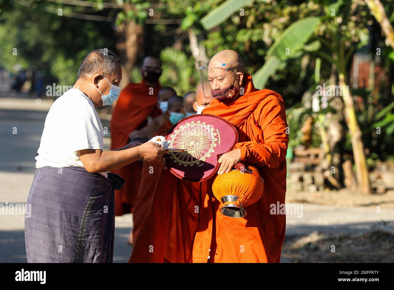 A Buddhist devotee donates alms to a Buddhist monk wearing a face ...