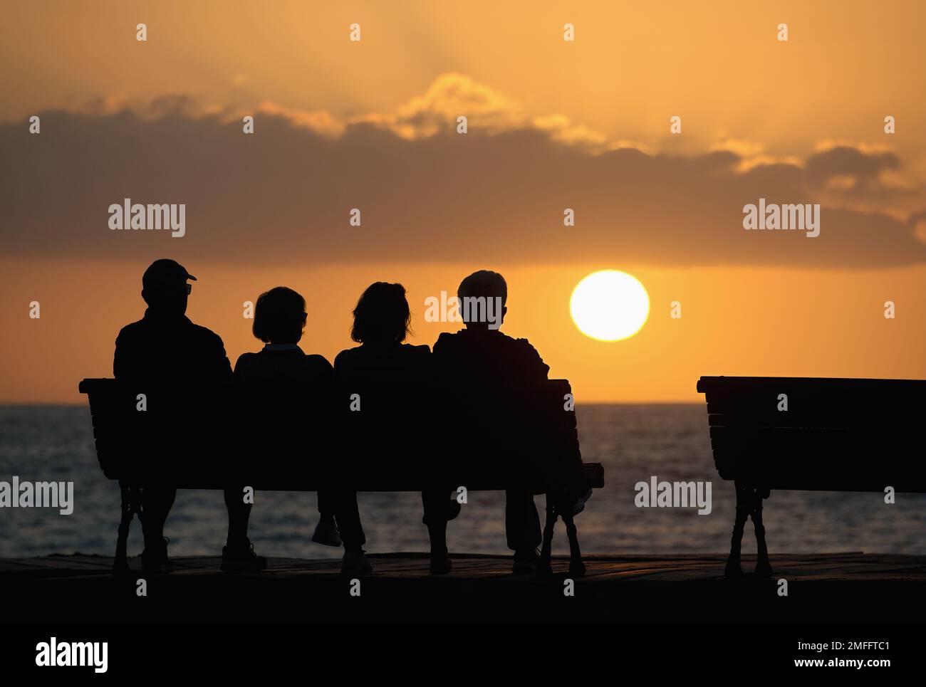 Silhouette of a group of seniors who sits on the bench, looking at the ...