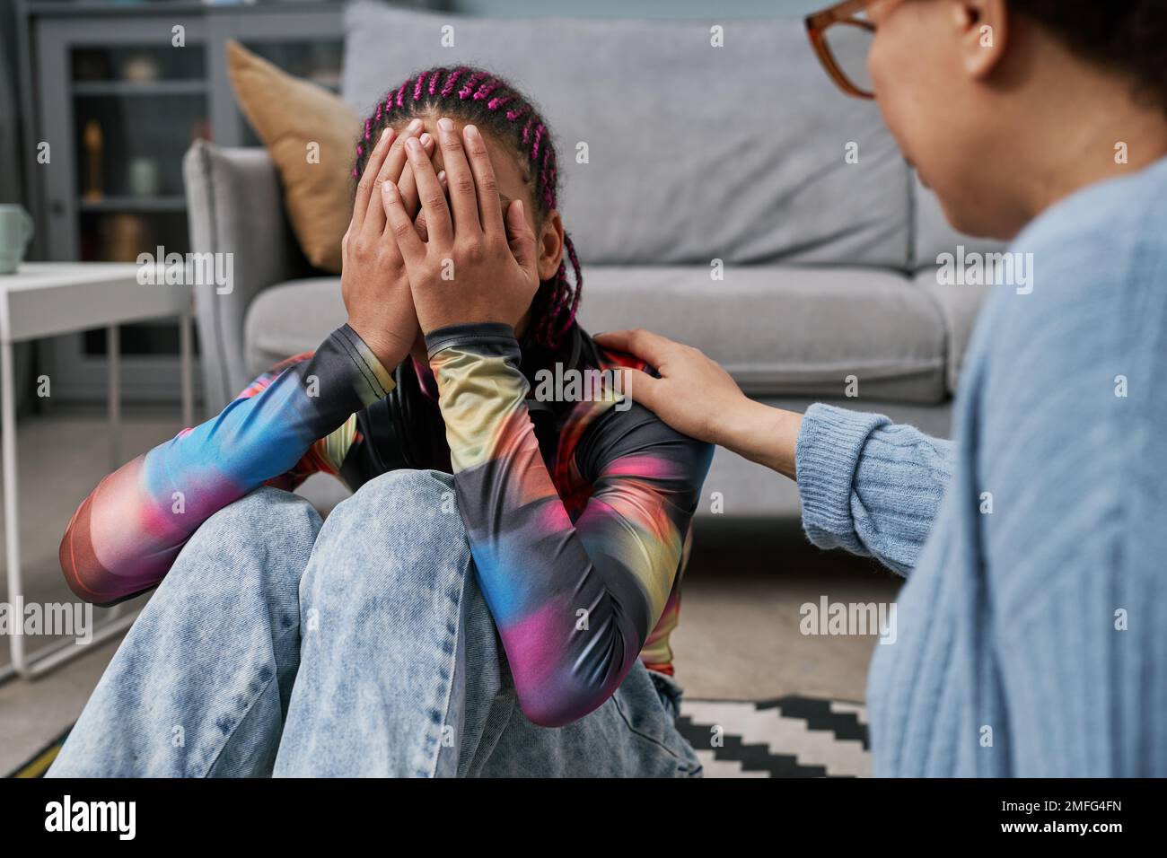 Portrait of crying teenage girl hiding face with mother or therapist ...
