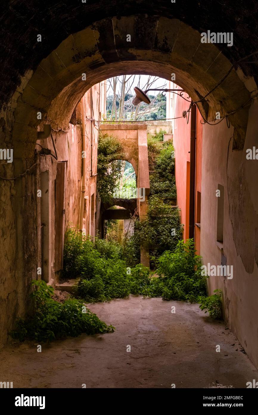 A small, ruined alley with archways, stone walls and overgrown stairs ...