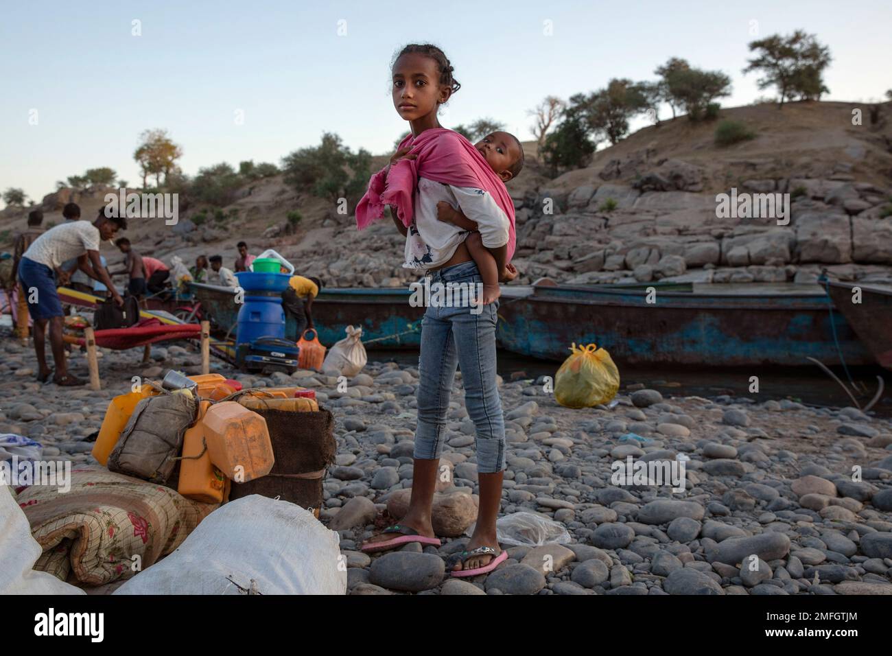Tigray refugee child carries a baby after they arrive on the banks of ...