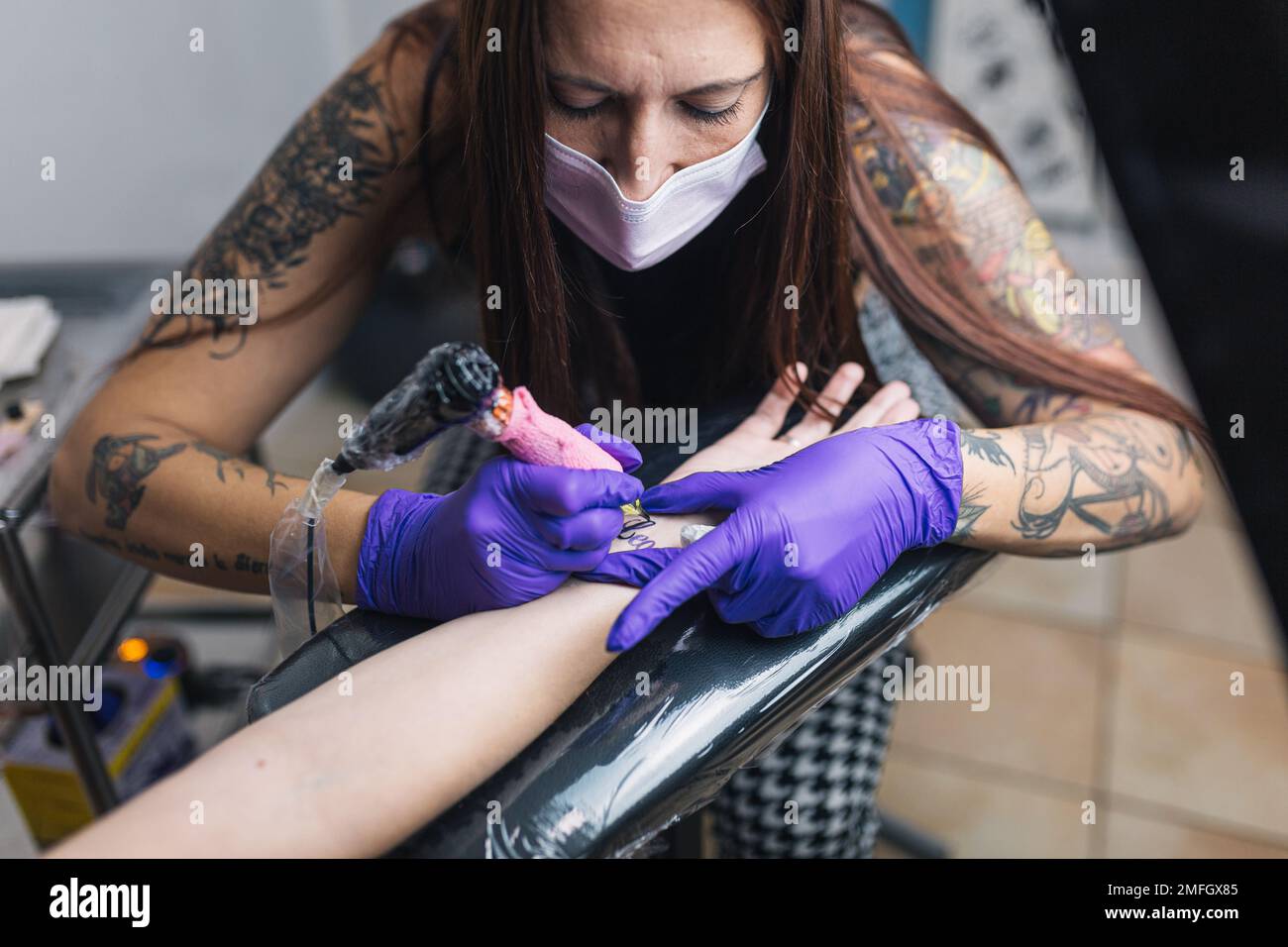 Tattoo artist tattooing in her studio with gloves and mask. Tattoo arm ...