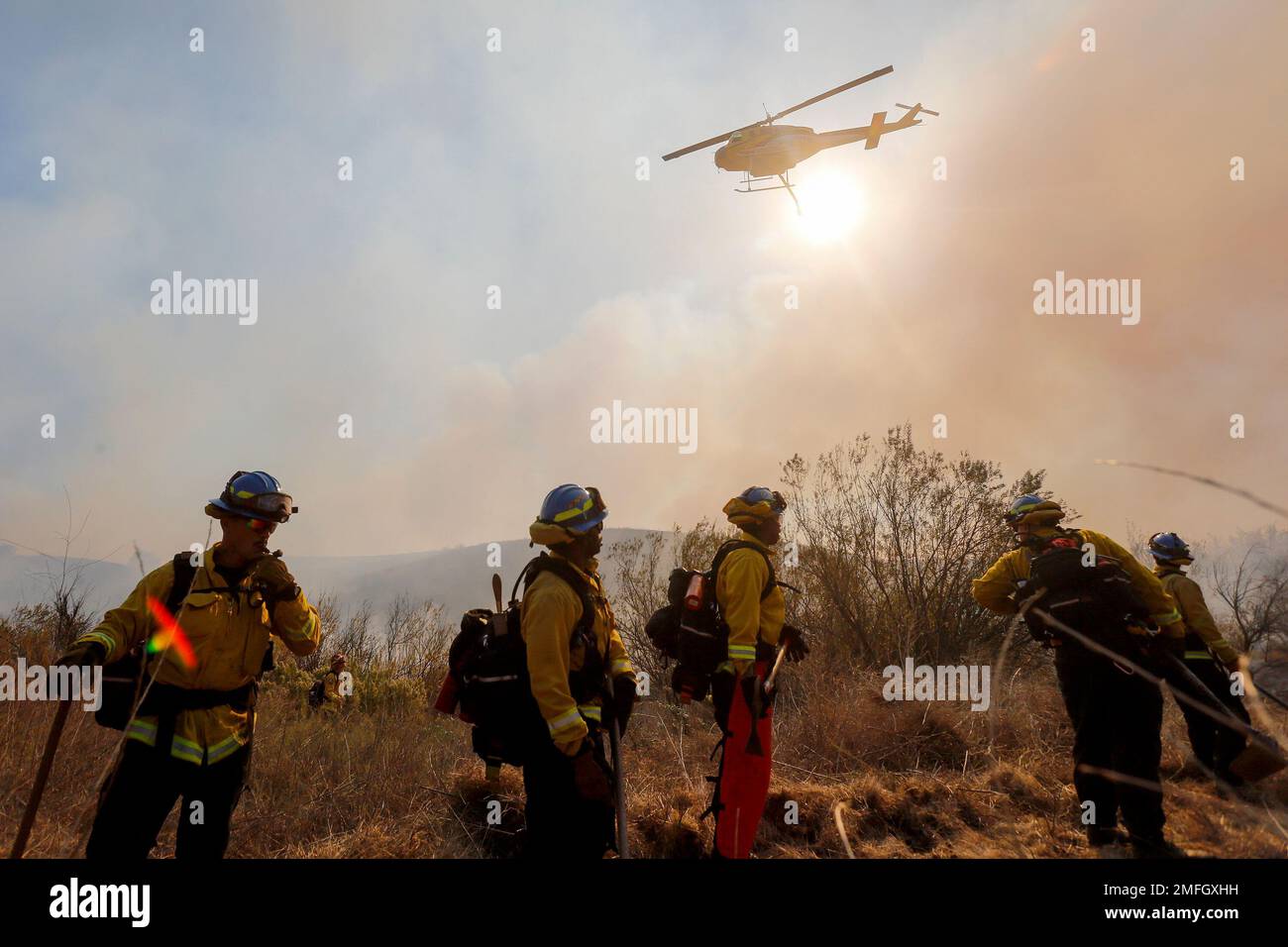A hotshot hand crew works on a fireline as a helicopter prepares to ...