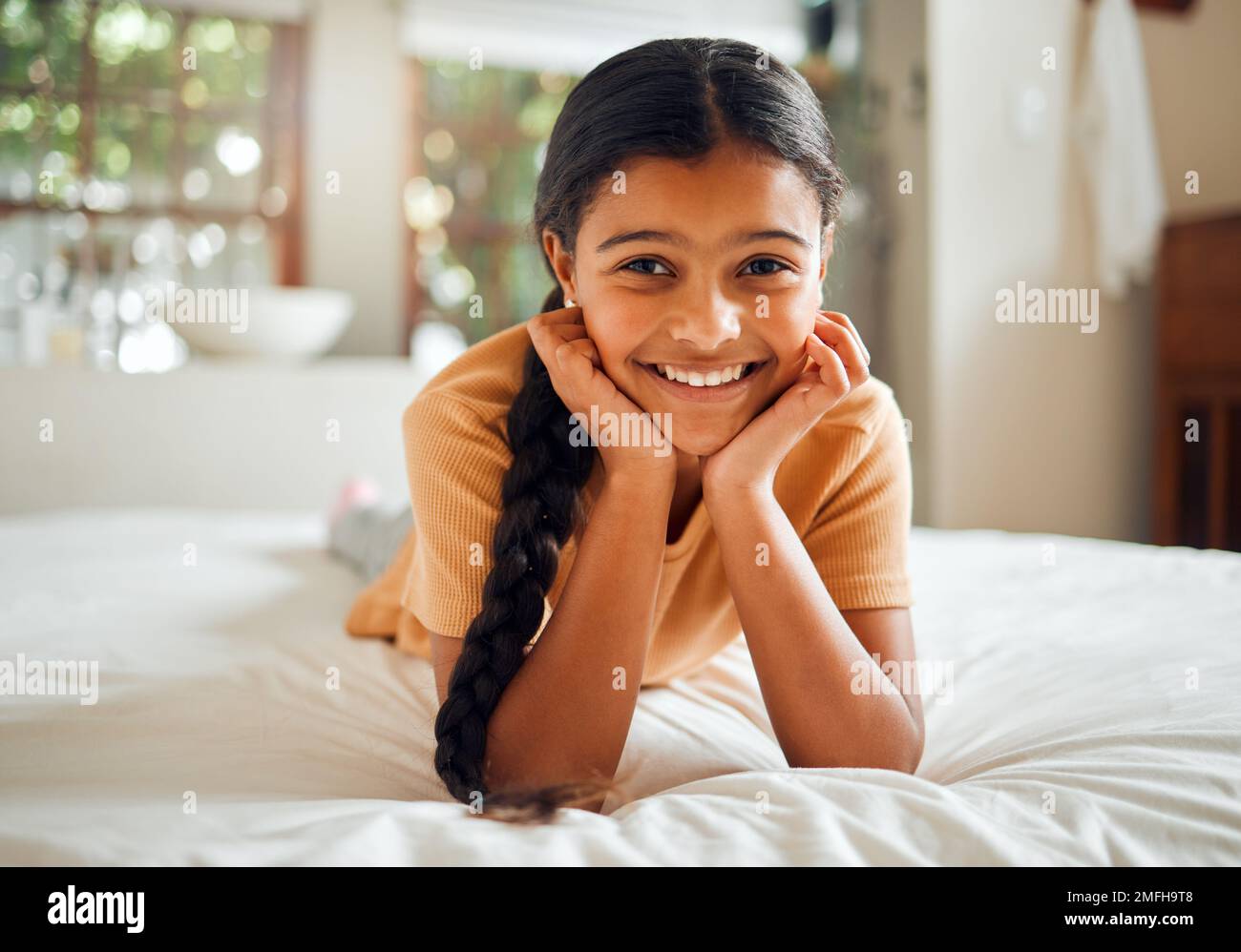 Portrait, children and bedroom with an indian girl lying on her bed at ...