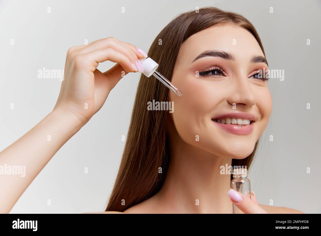 Attractive young girl with well-kept healthy skin applying face serum ...