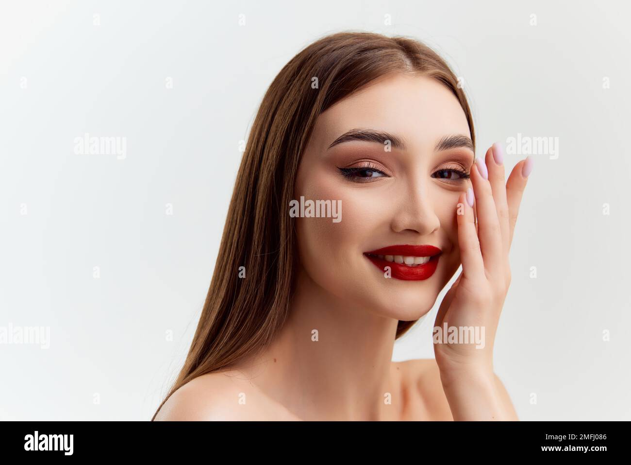 Tender make-up look. Young beautiful brunette girl with red lips makeup posing over grey studio ...