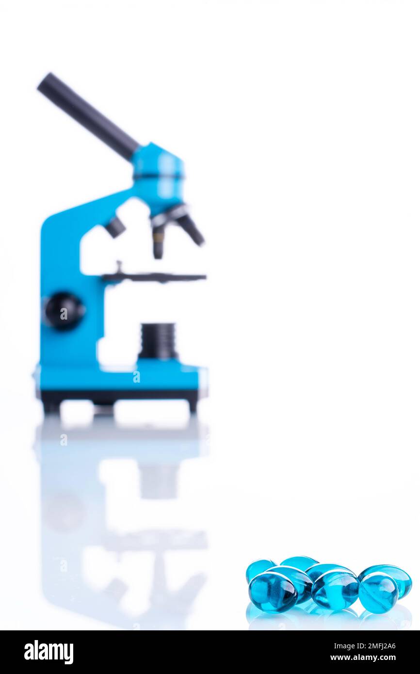 A vertical shot of blue vitamin capsules with a microscope on white ...