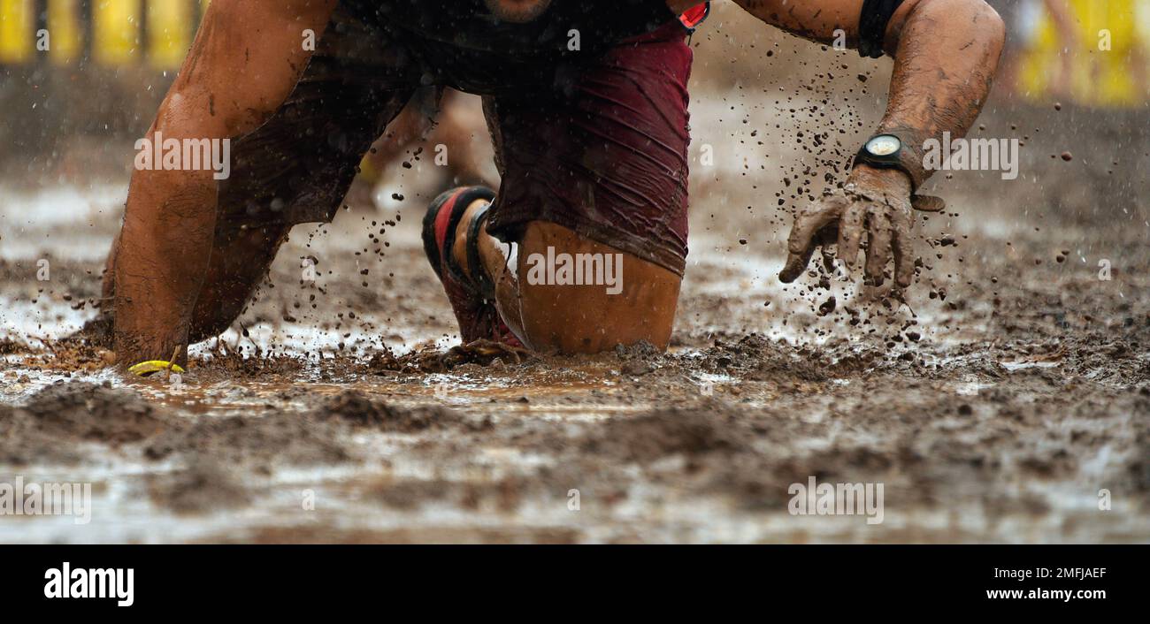 Mud race runners. Crawling,passing under a barbed wire obstacles during ...