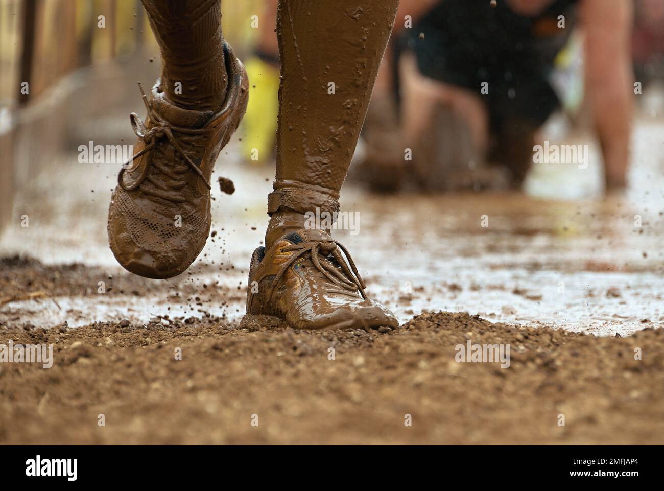 Mud race runners passing under a barbed wire obstacles during extreme ...