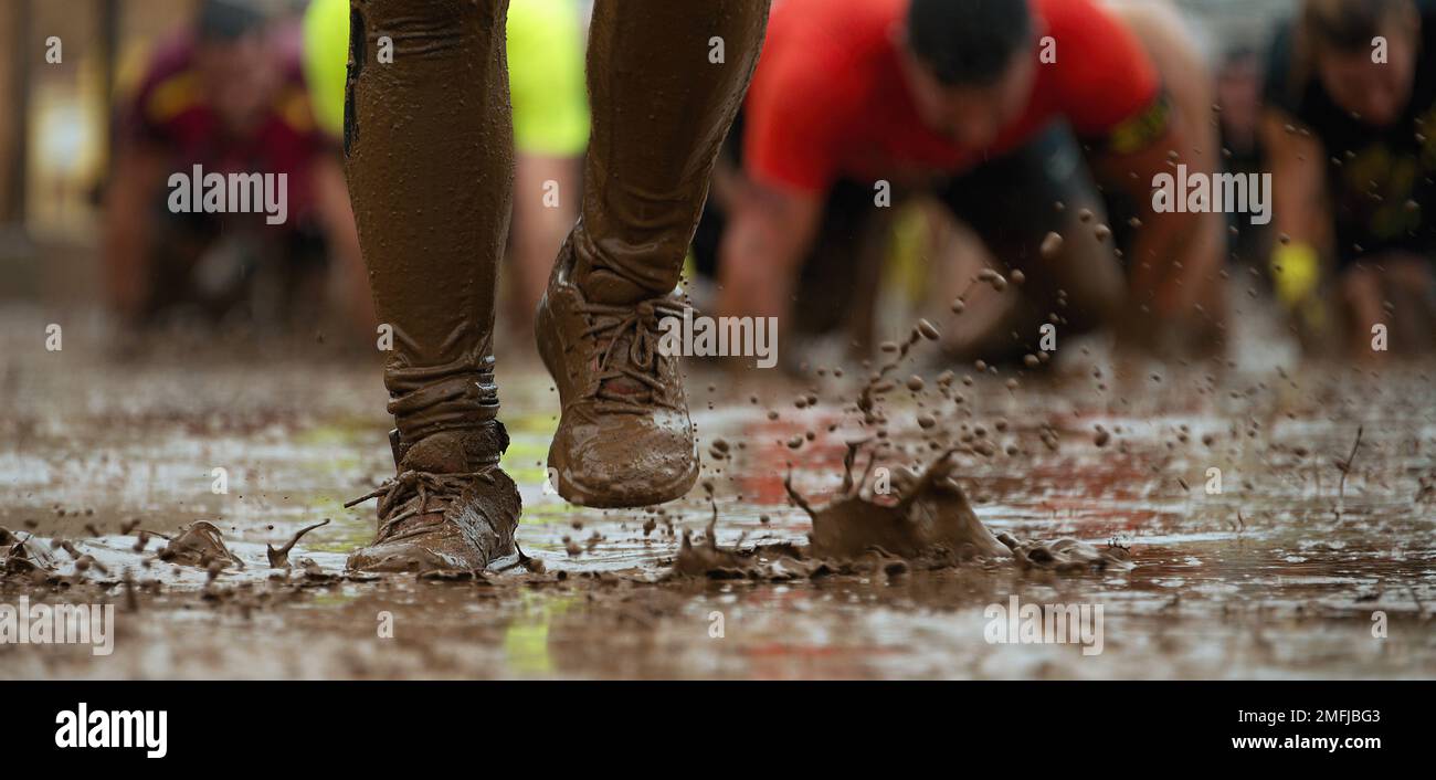 Mud race runners passing under a barbed wire obstacles during extreme ...
