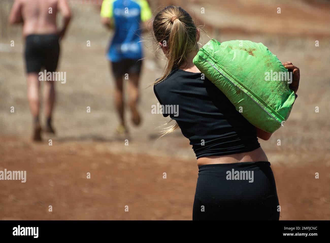 Mud race runners, young woman running with sandbag Stock Photo - Alamy