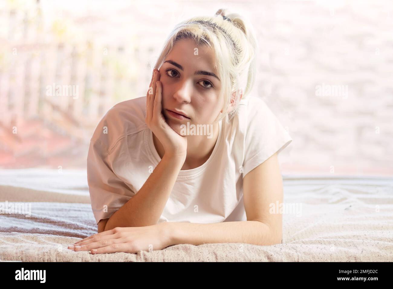 blonde girl with hand on chin stretched out on bed with a sad face ...