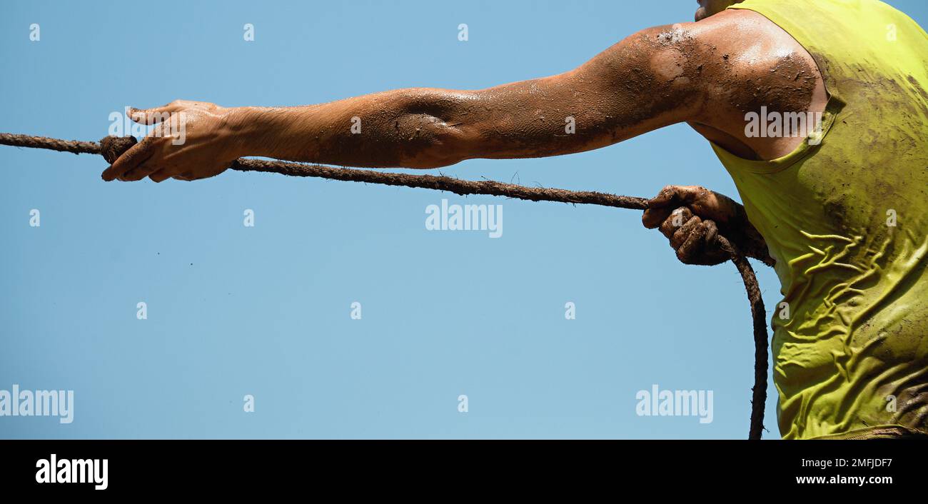 Mud race runners,defeating obstacles by using ropes Stock Photo - Alamy
