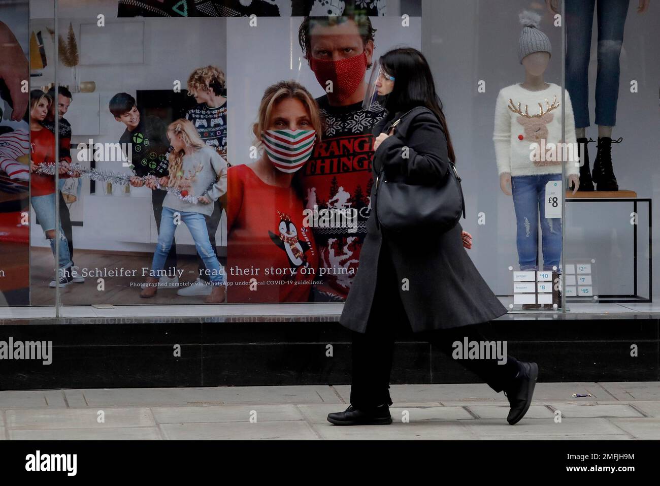 A woman wearing a face shield walks past the front window of the ...