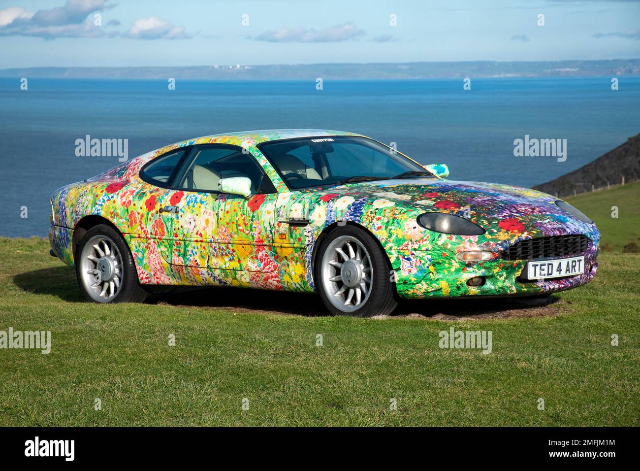 Jaguar car painted in psychedelic colours, standing on a clifftop ...