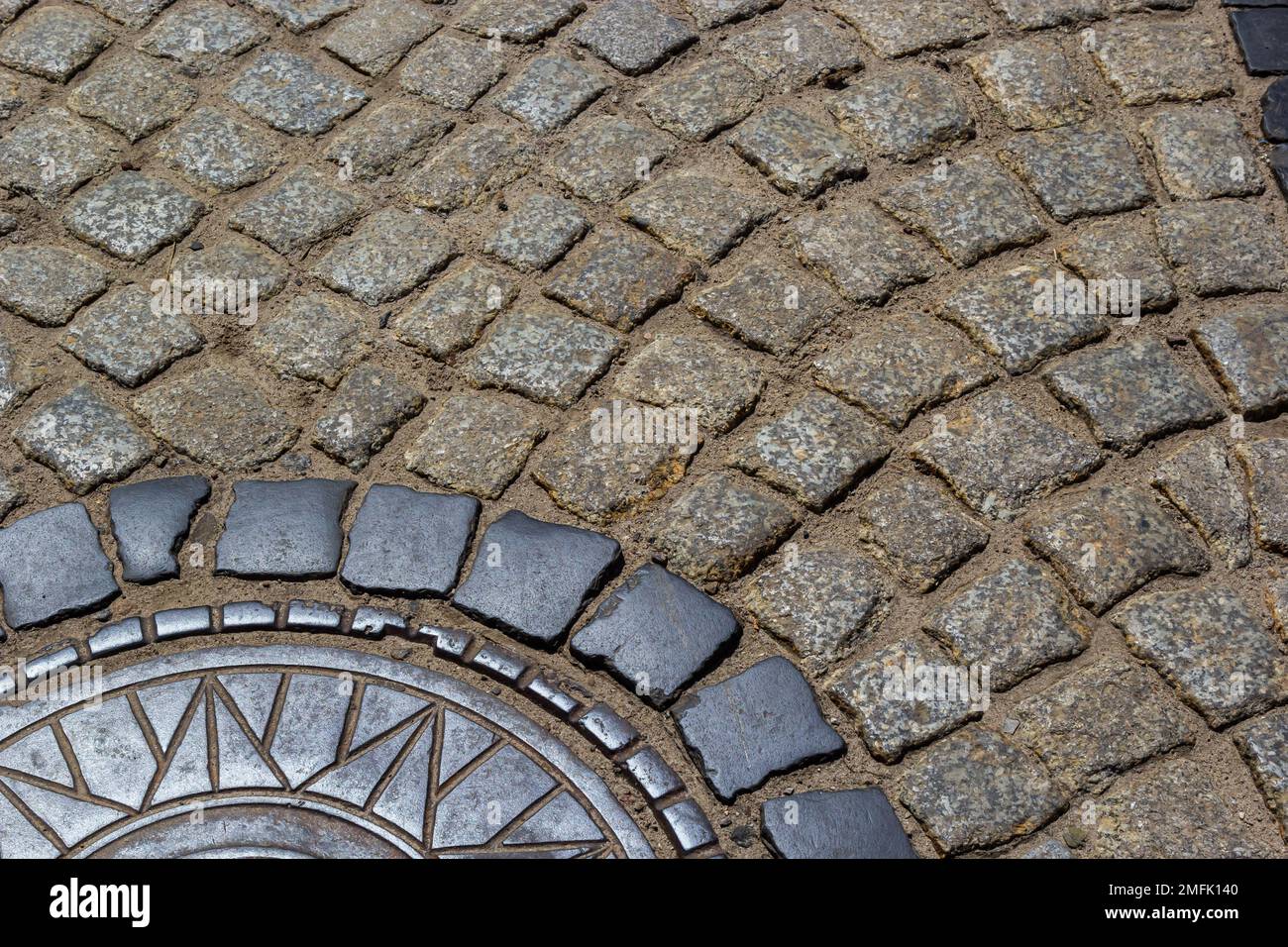 Old metal sewer hatch in the middle of the road, laid out of a smooth ...