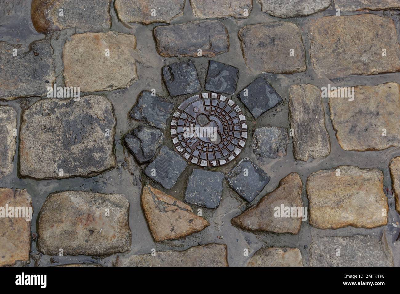 Old metal sewer hatch in the middle of the road, laid out of a smooth ...