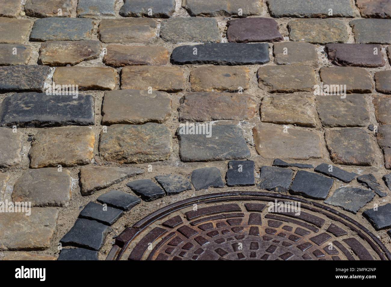 Old metal sewer hatch in the middle of the road, laid out of a smooth ...