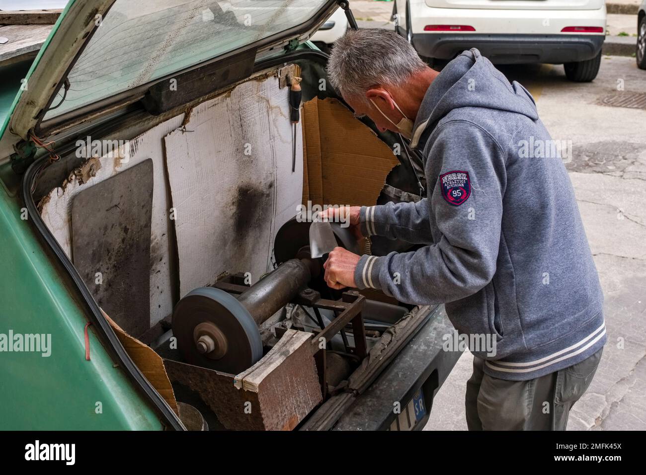 A knife grinder grinds knives in the trunk of his car in the streets of ...