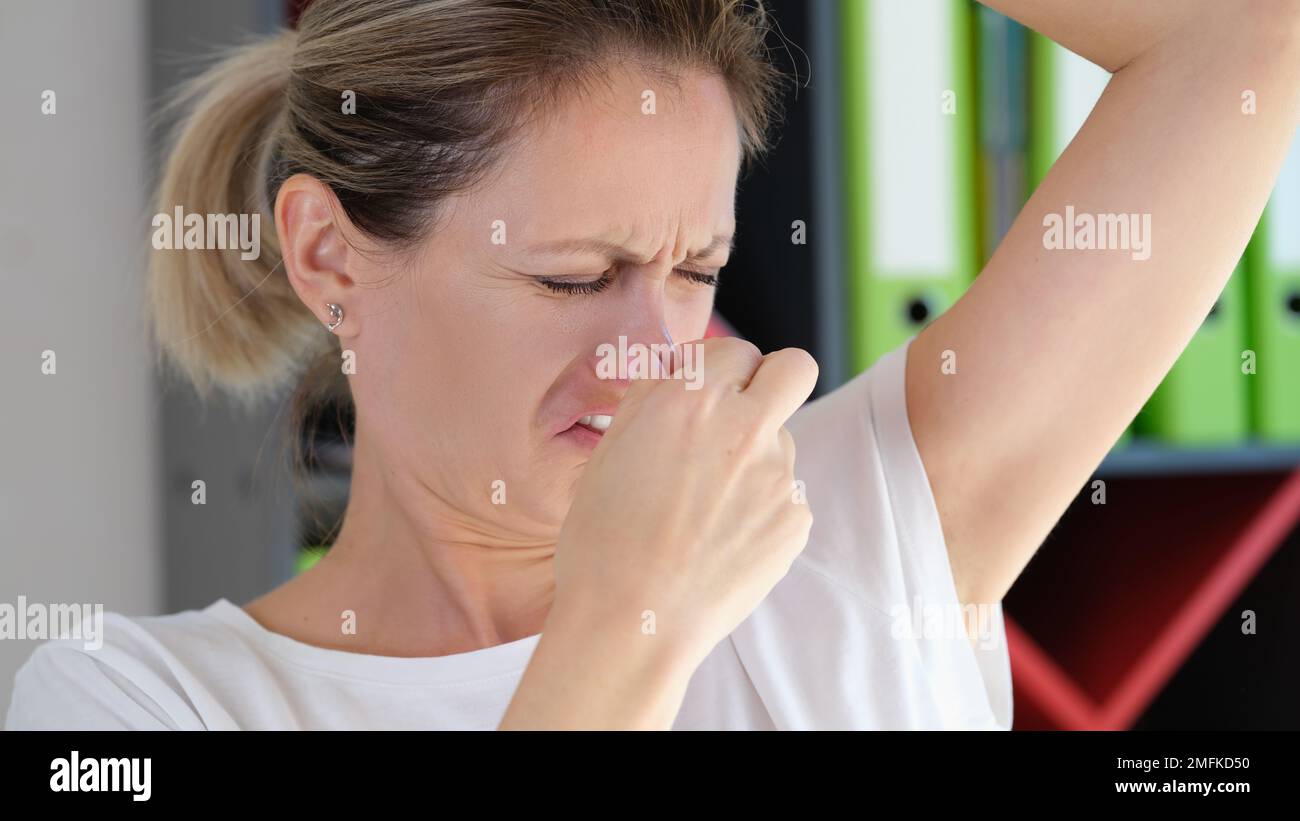 Worried woman with unhappy face checking smell of her armpit in office ...