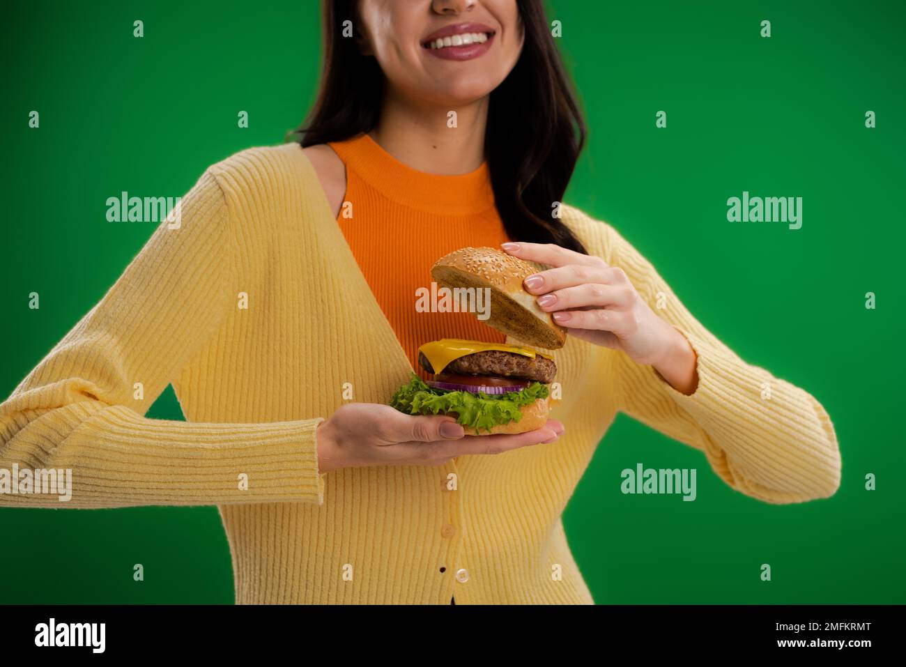 cropped view of smiling woman holding burger with meat and cheese with ...