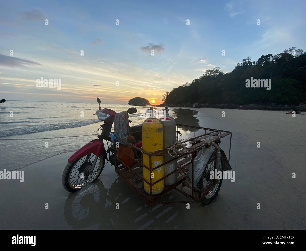 A motorbike with gas cylinders in a sidecar on a sandy beach at sunset ...