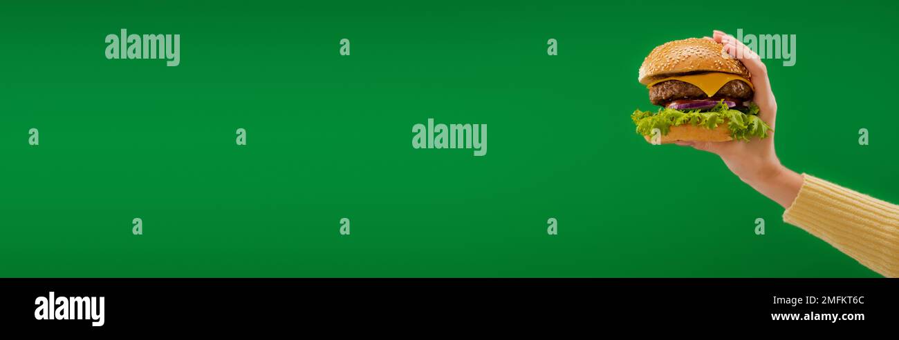 cropped view of woman holding burger with cheese and meet with lettuce ...