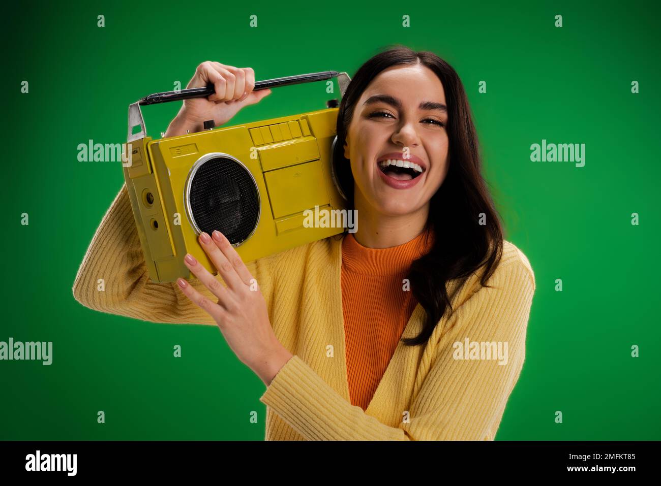 excited brunette woman holding boombox and laughing at camera isolated ...