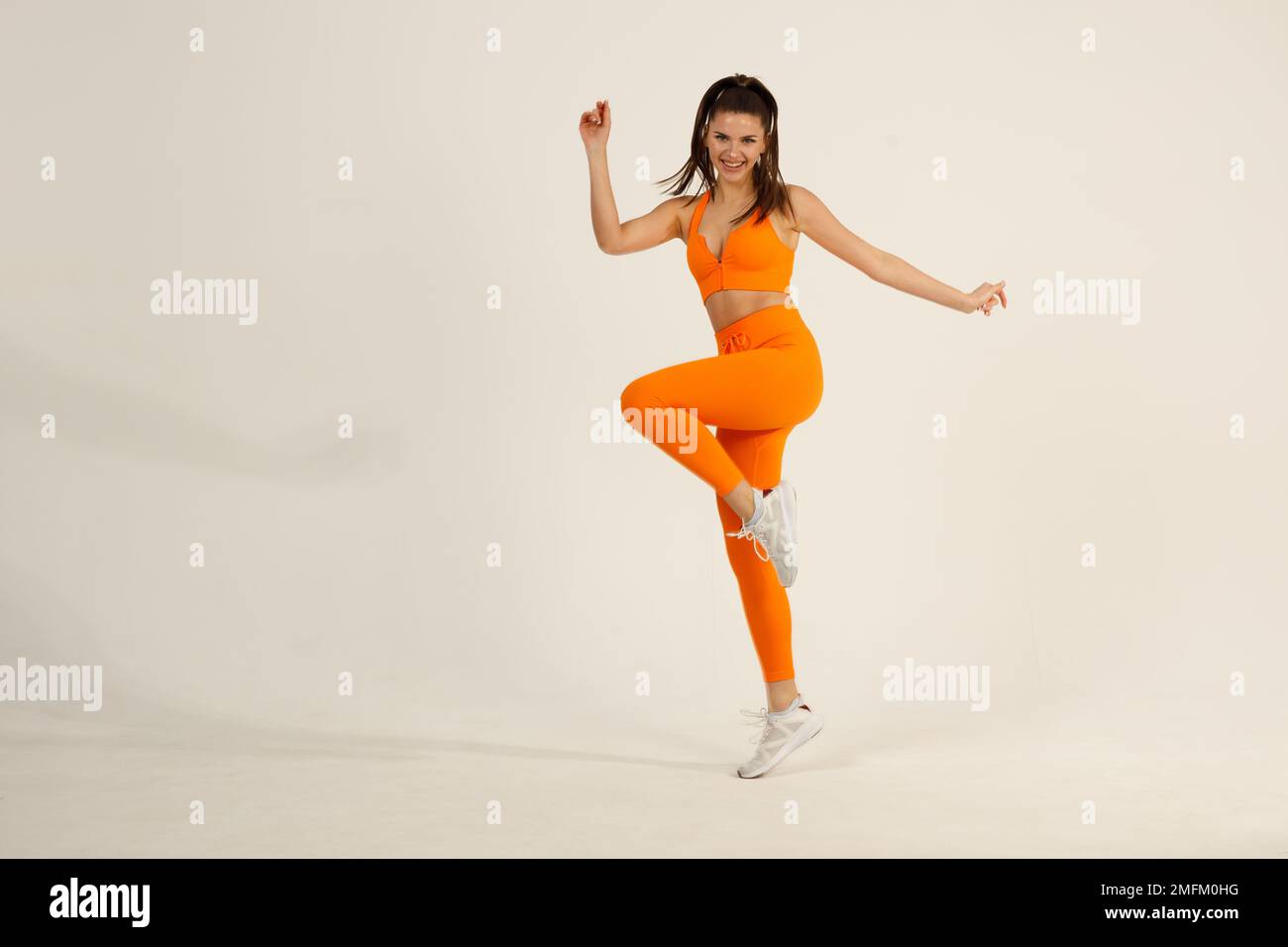 Young positive smiling woman dancing step excercise in orange fitness ...