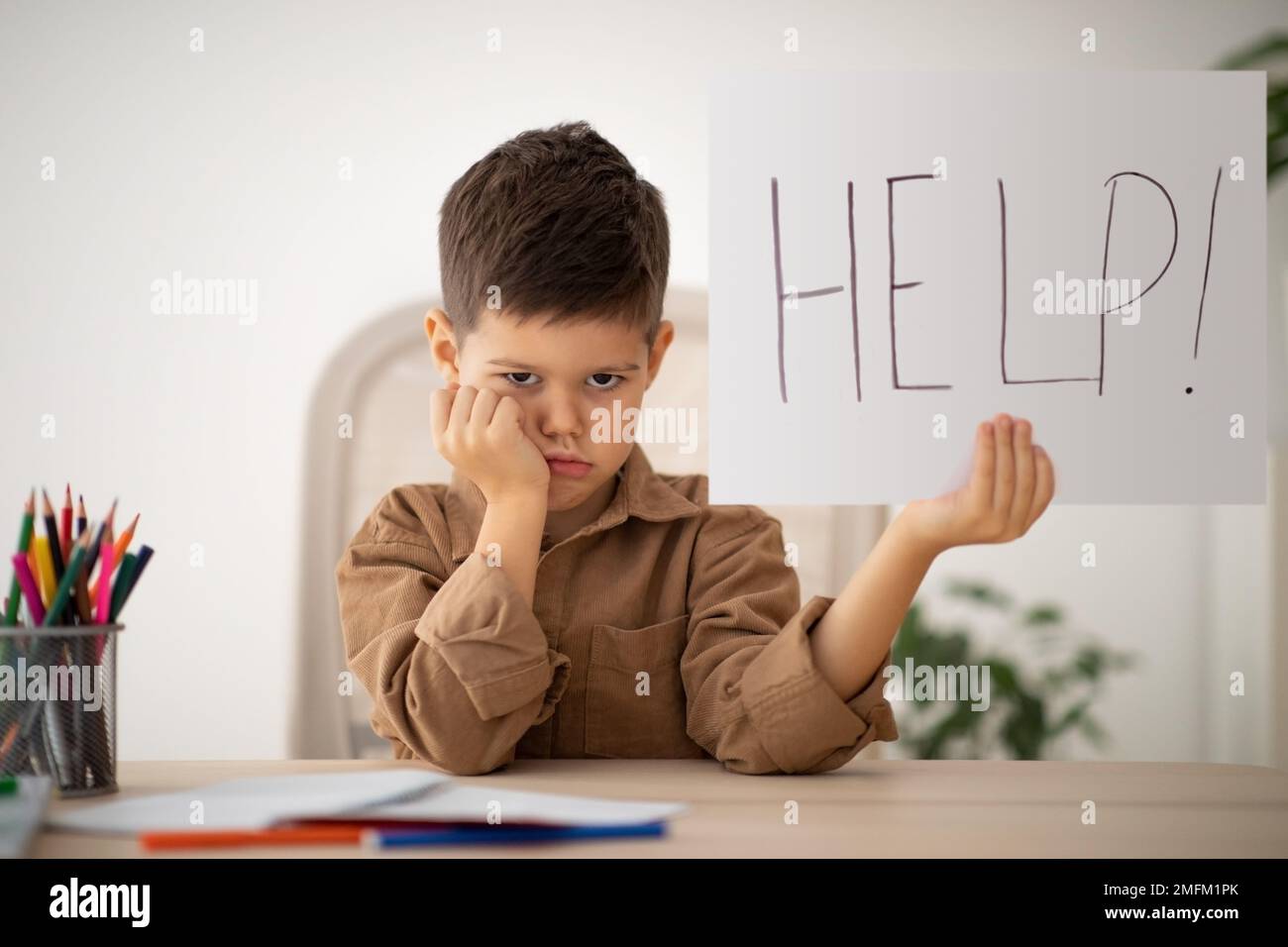 Sad unhappy little boy sits at table, studies and shows banner with ...