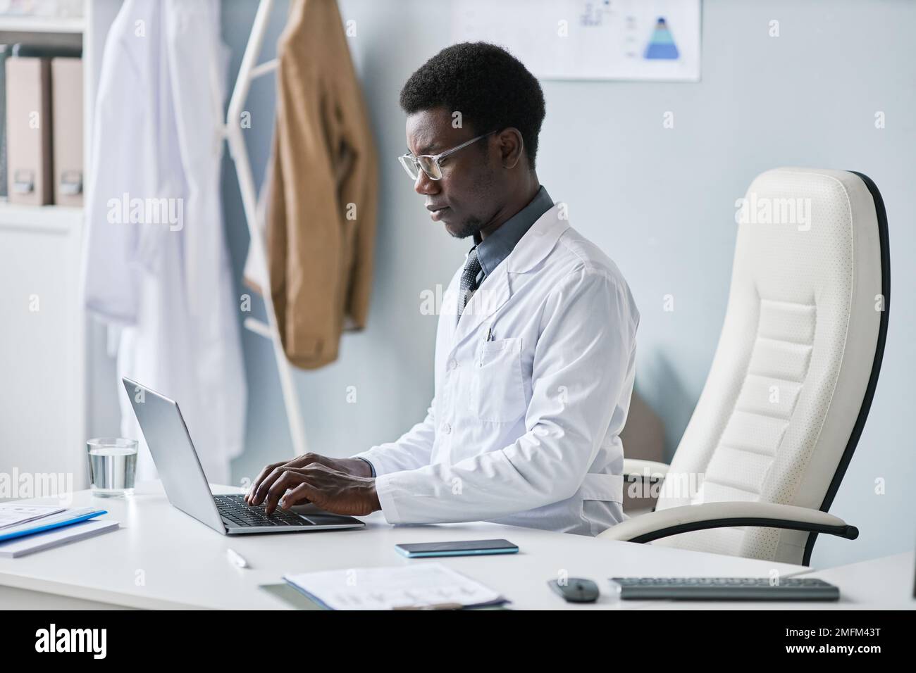 Minimal side view portrait of young black doctor using laptop in office ...