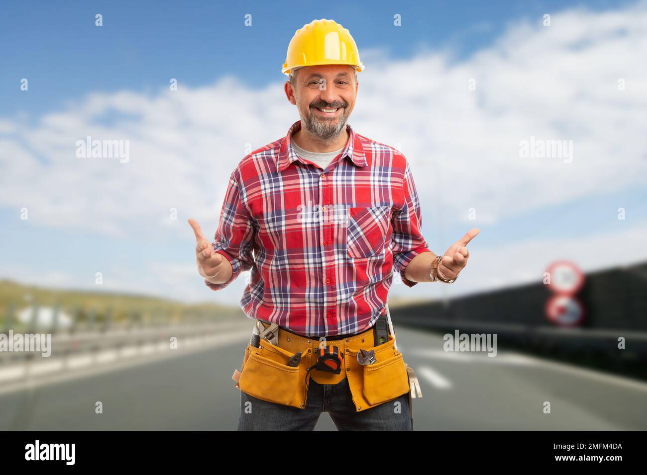 Happy worker with yellow helmet making thumbs-up gesture on highway as ...