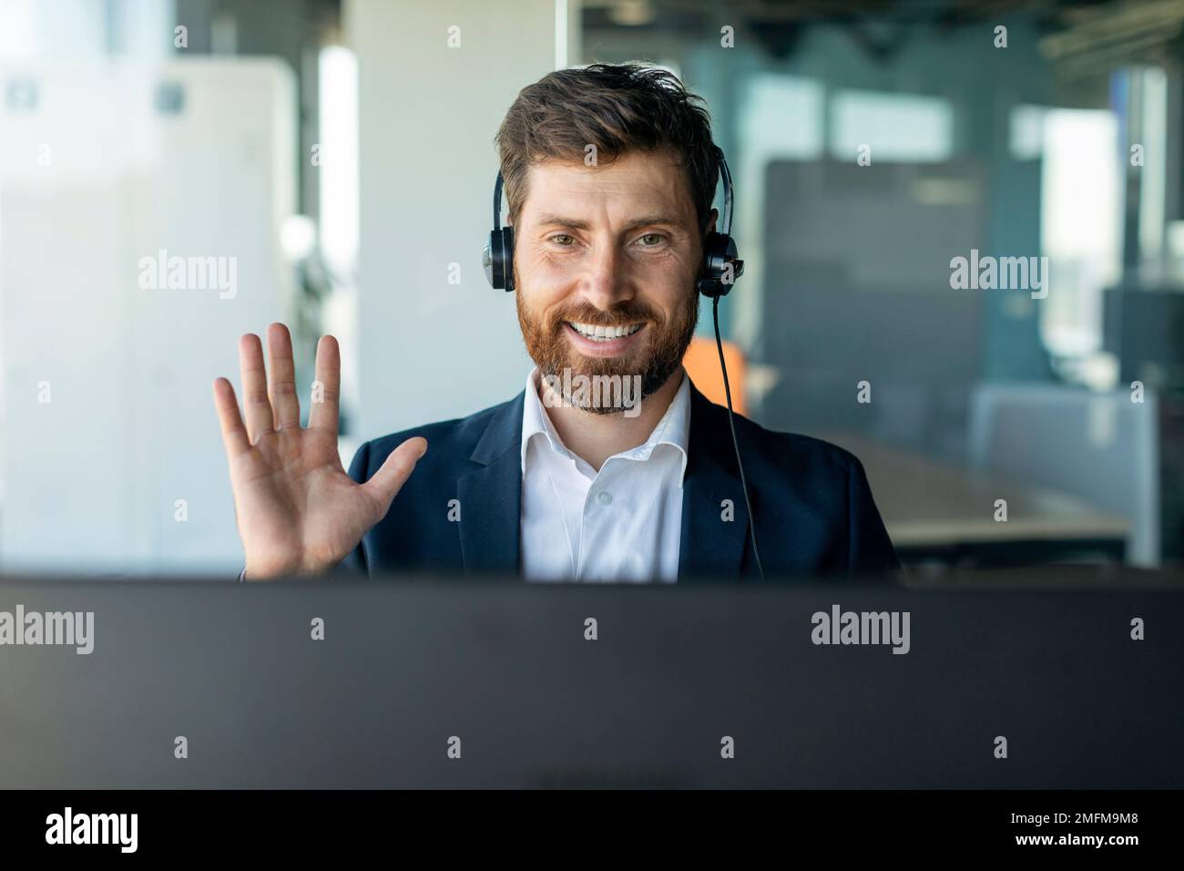 Happy middle aged businessman in headphones waving hand at computer ...