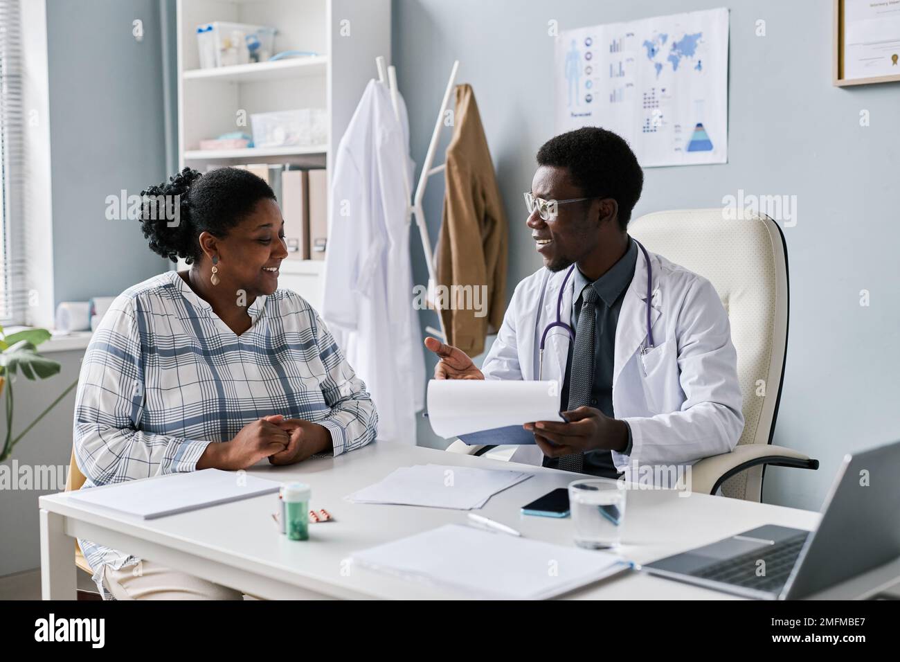 Portrait of young black doctor talking to young woman during ...