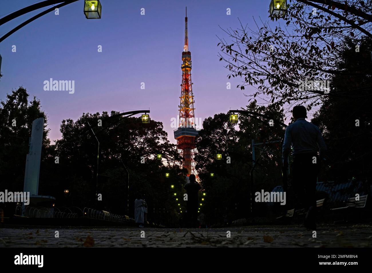 Tokyo Tower is lit up against the sunset sky as people stop to take ...