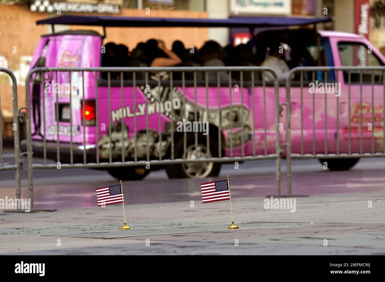 A Hollywood tour bus passes by in the background as American flags are ...