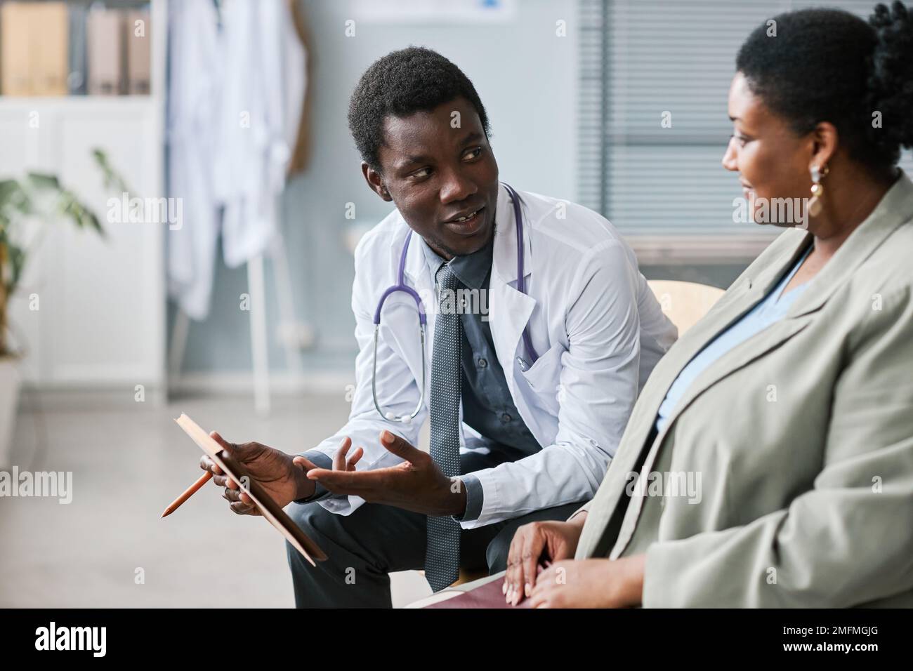 Portrait of black young man as doctor consulting female patient in ...