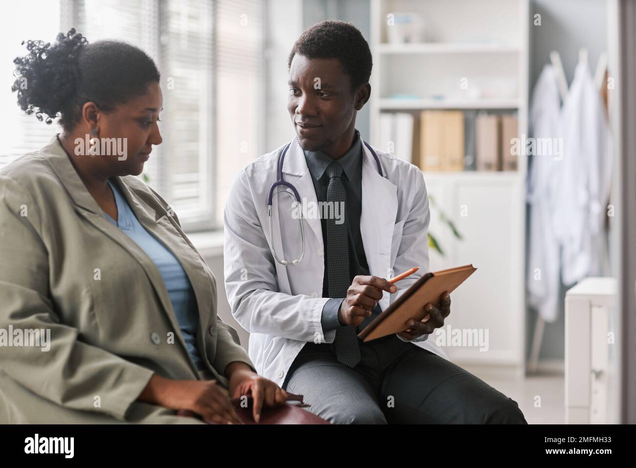 Portrait of black young man as doctor consulting woman in clinic and ...